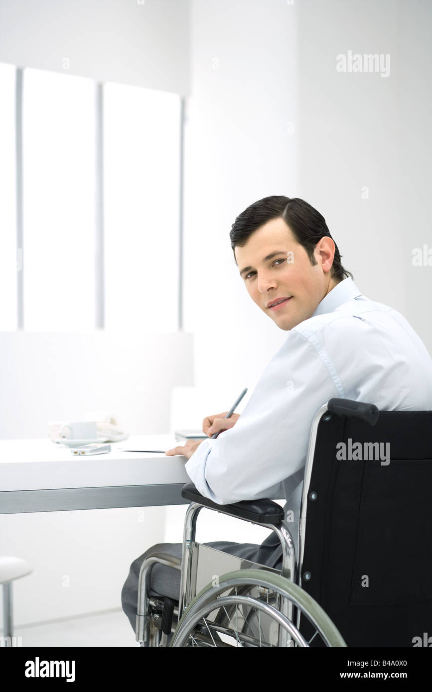 Professional man in wheelchair working at desk, smiling over shoulder ...