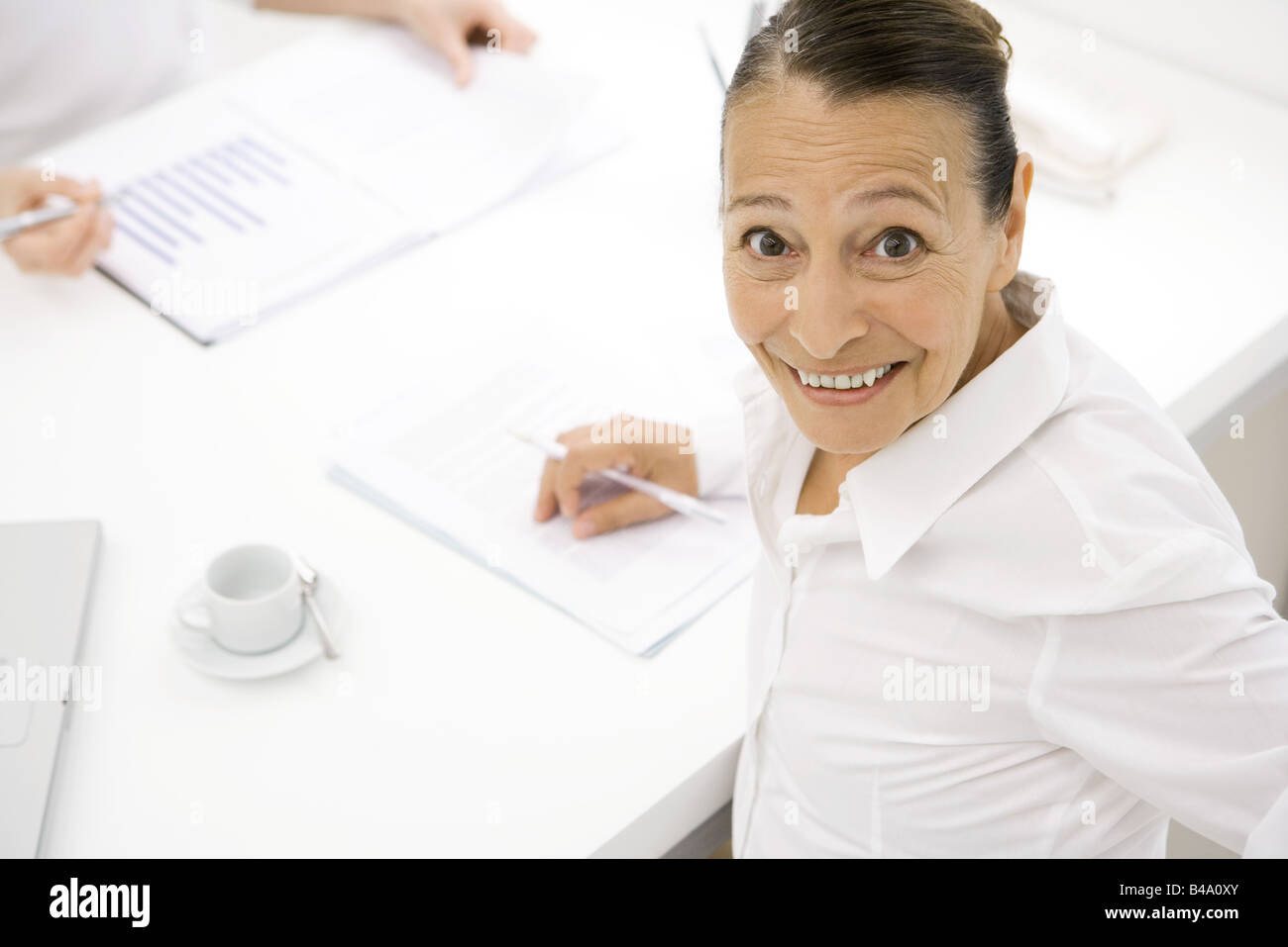 Senior woman working at table, smiling up at camera Stock Photo - Alamy
