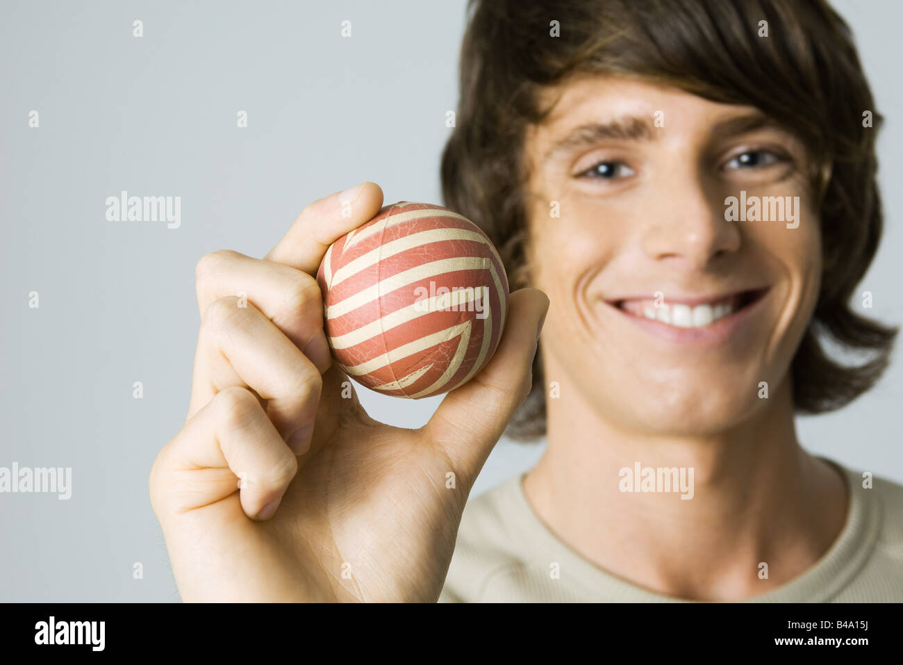 Young man holding striped ball, smiling at camera Stock Photo - Alamy