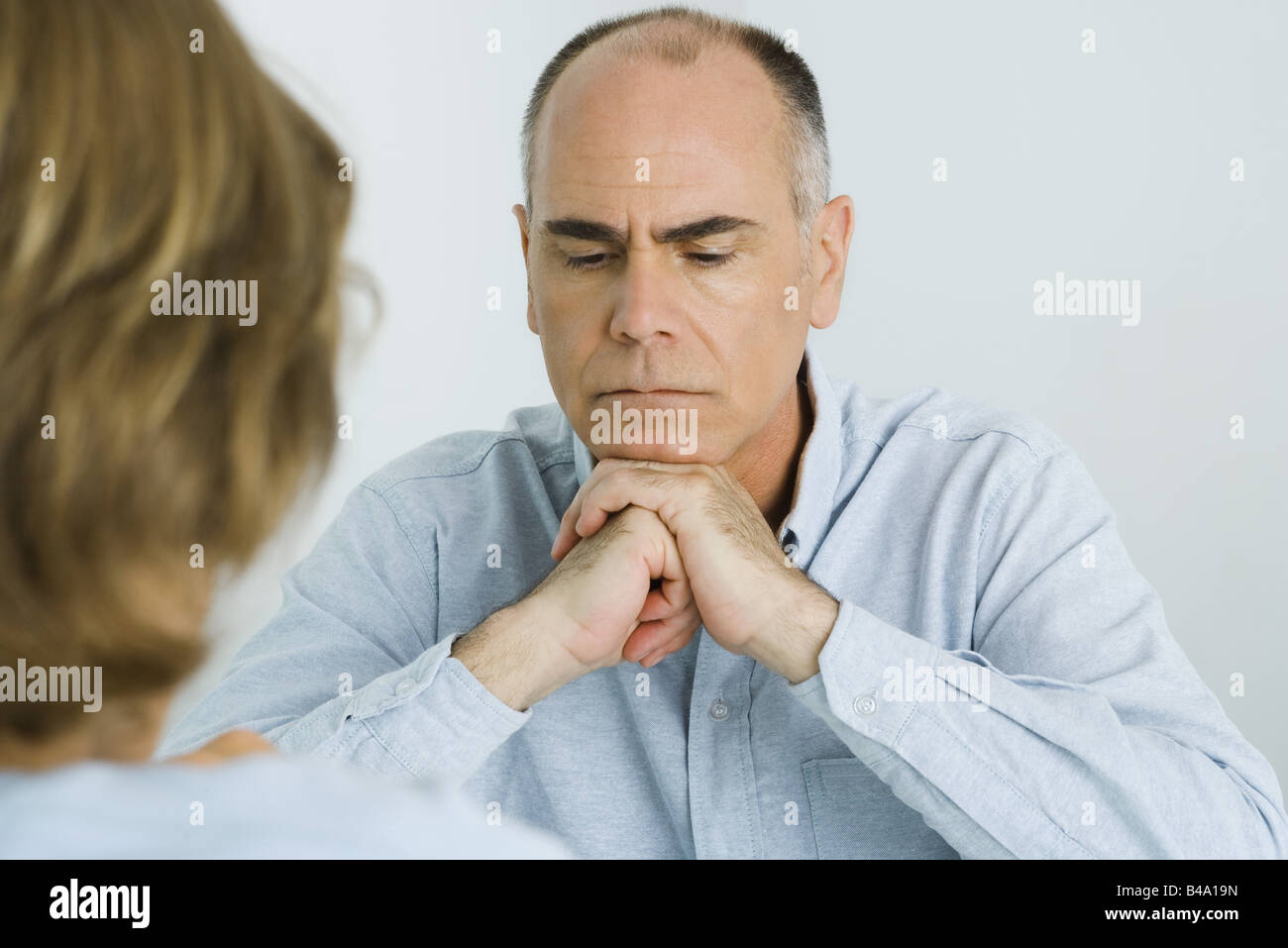 Man resting chin on clasped hands, looking down, over the shoulder view ...
