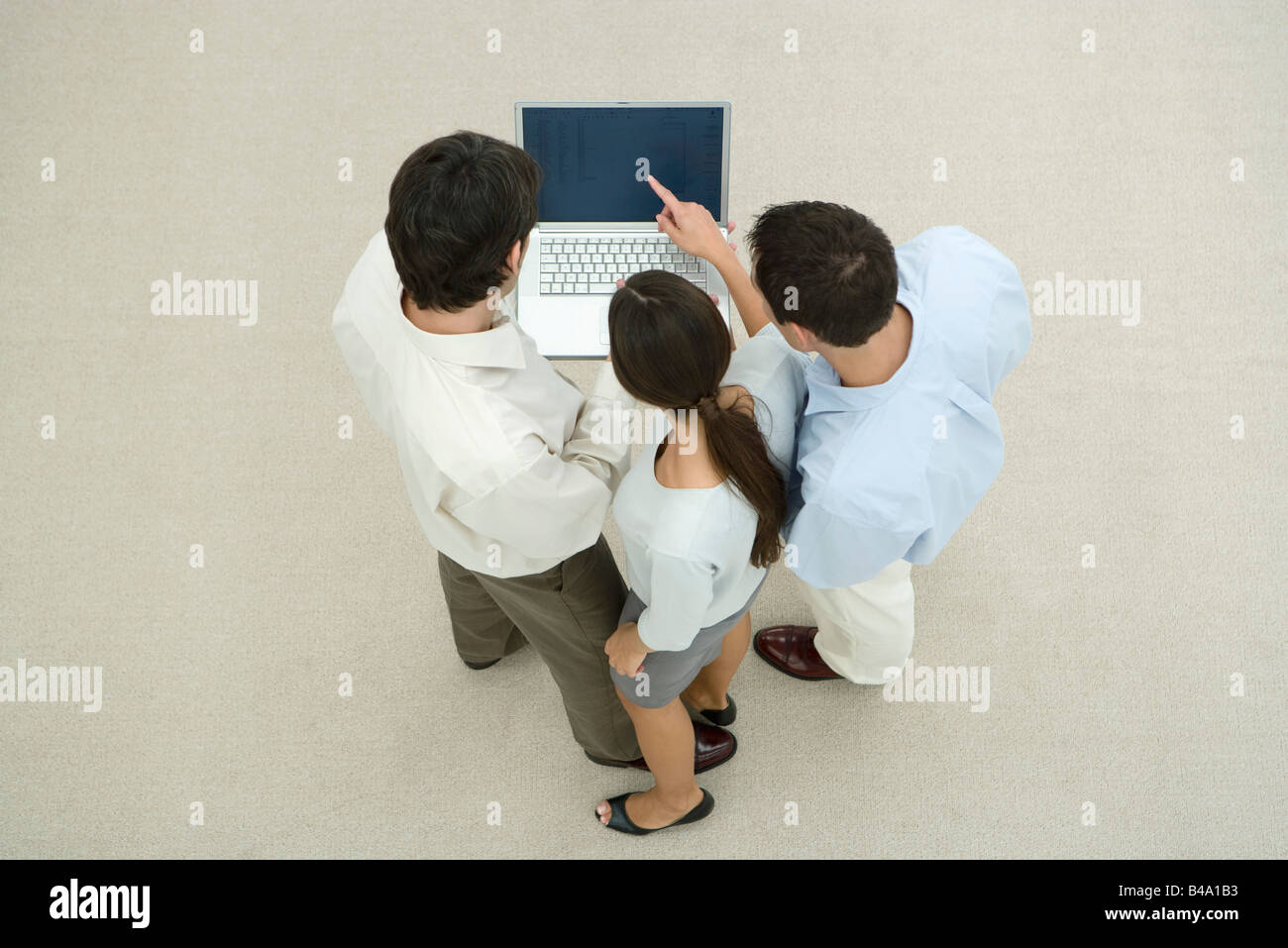 Three professionals standing, looking at laptop computer together, high ...