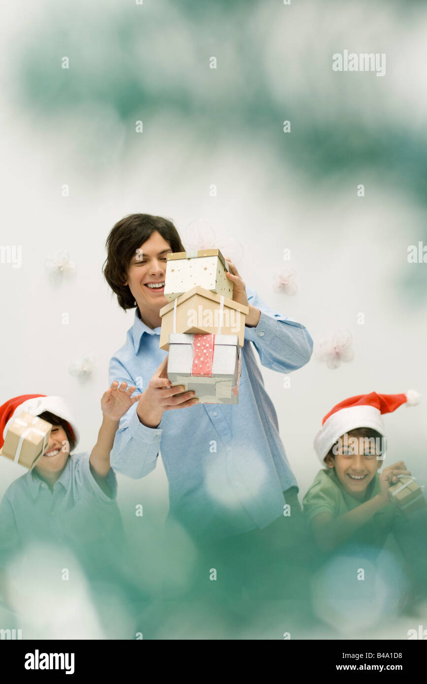 Young man holding stack of presents, boys wearing Santa hats catching ...