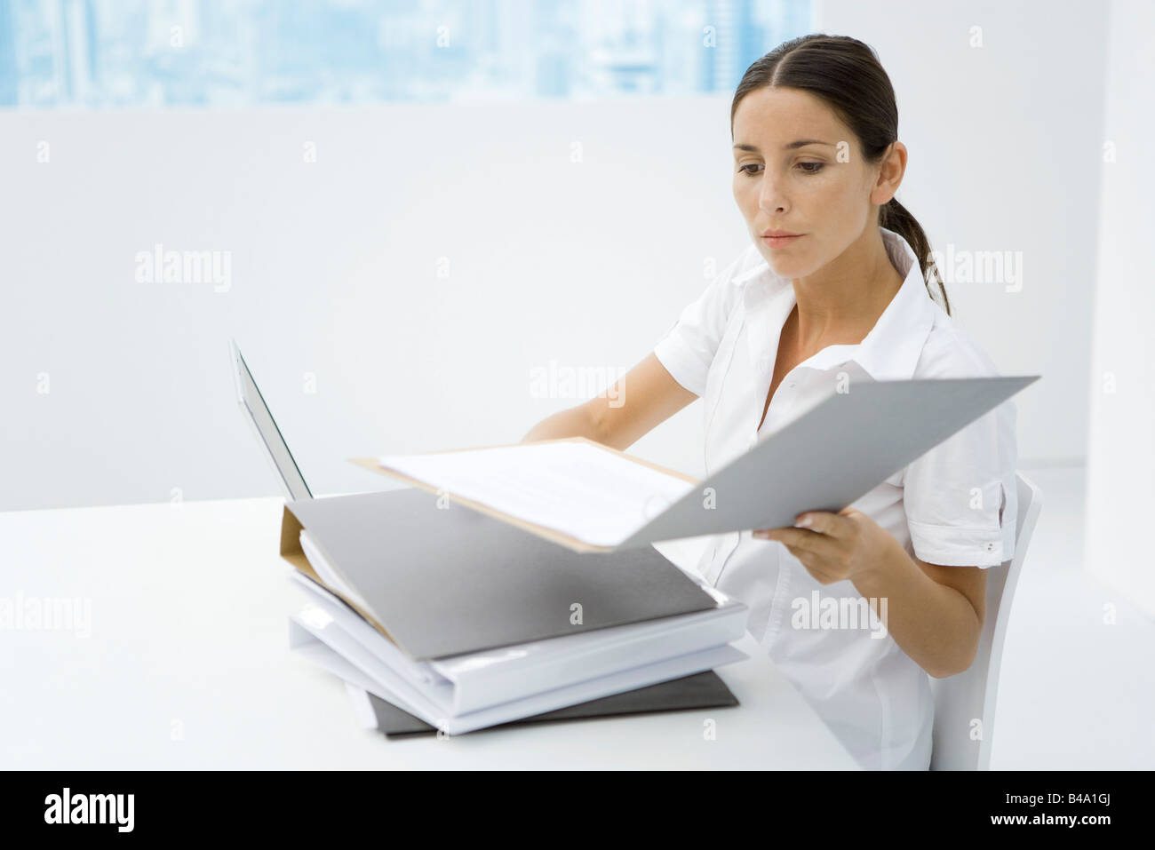 Woman sitting at desk, looking at stacked binders Stock Photo - Alamy