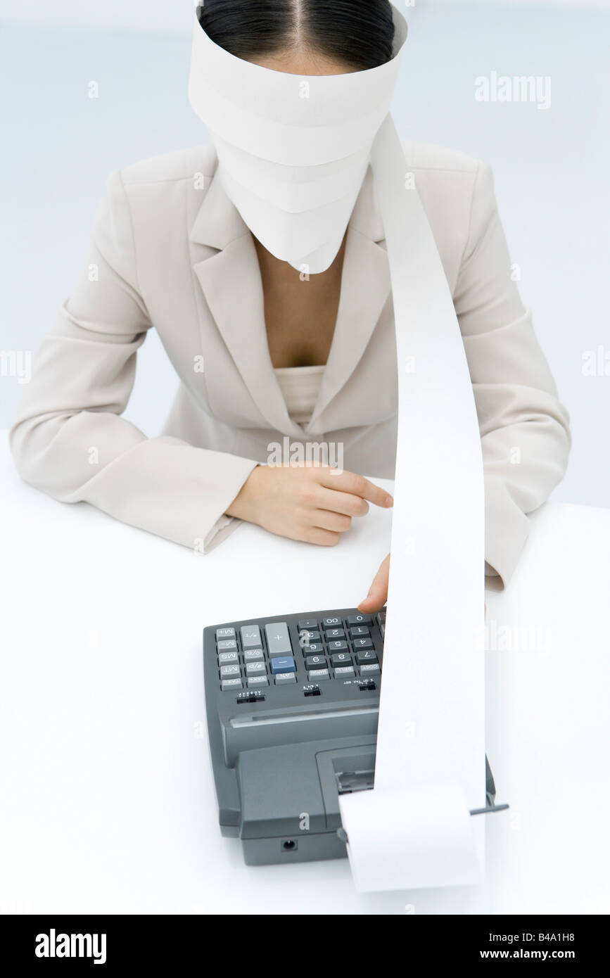 Businesswoman using adding machine, blindfolded with paper printout ...