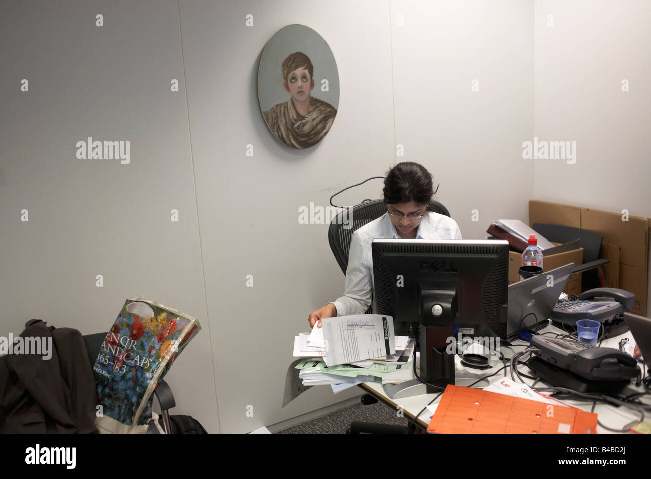 A casually-dressed accountant works in a cluttered office cubicle in an ...