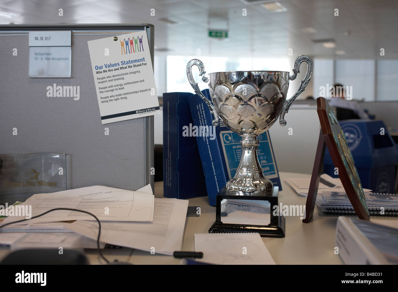 Office worker's cluttered desk with trophy shield and company statement ...