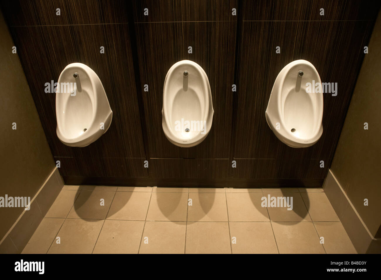 Three clean office urinal toilets fixed to dark wooden panelling in ...