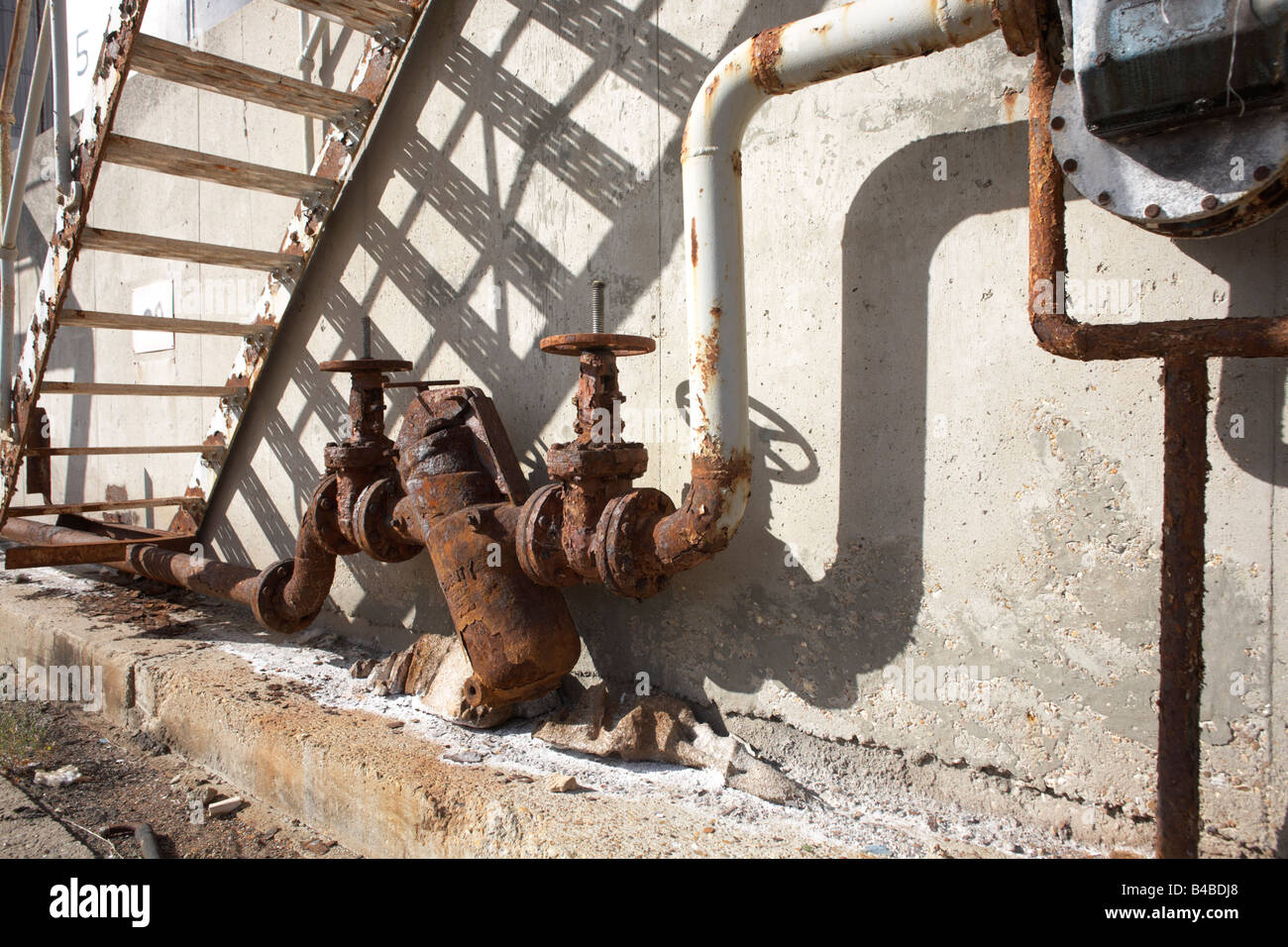 The shadows of rusting industrial pipes and gate valves on abandoned ...