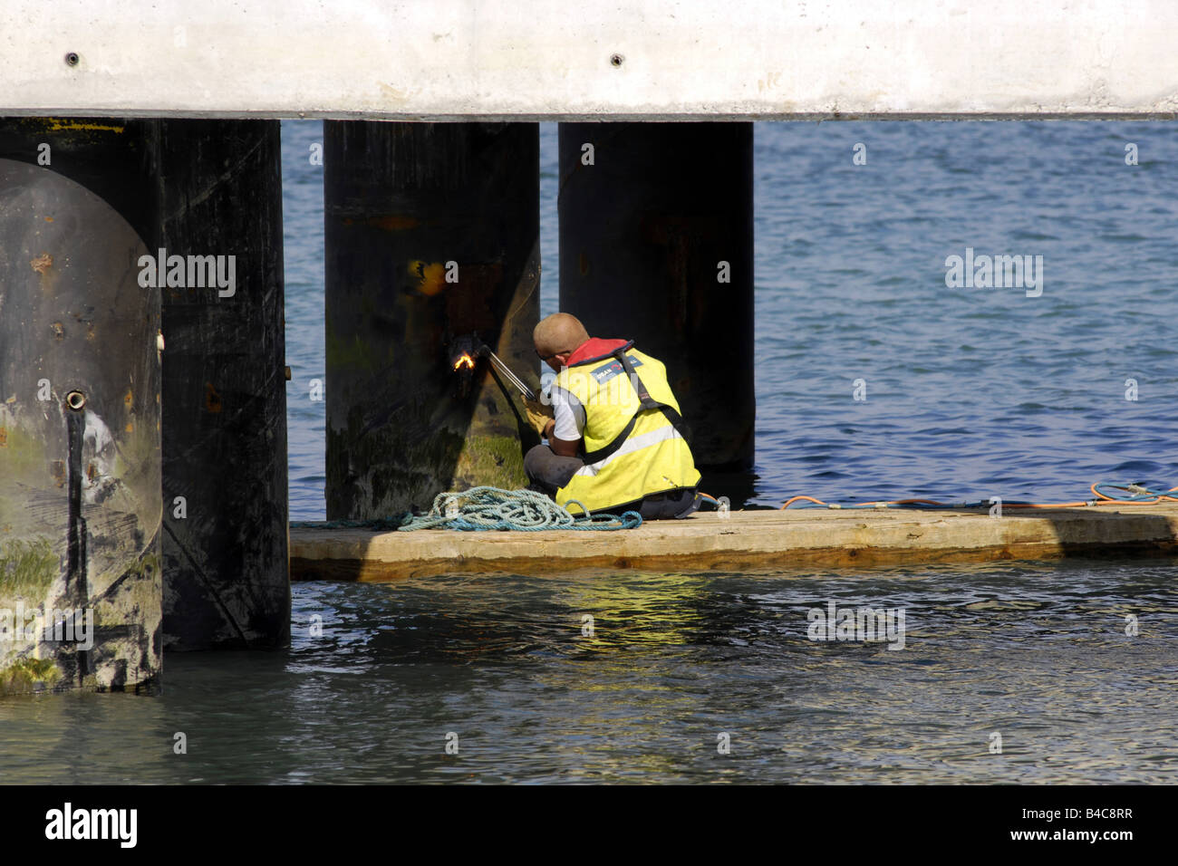 Workman sitting on a small raft using an gas torch to cut and weld a ...
