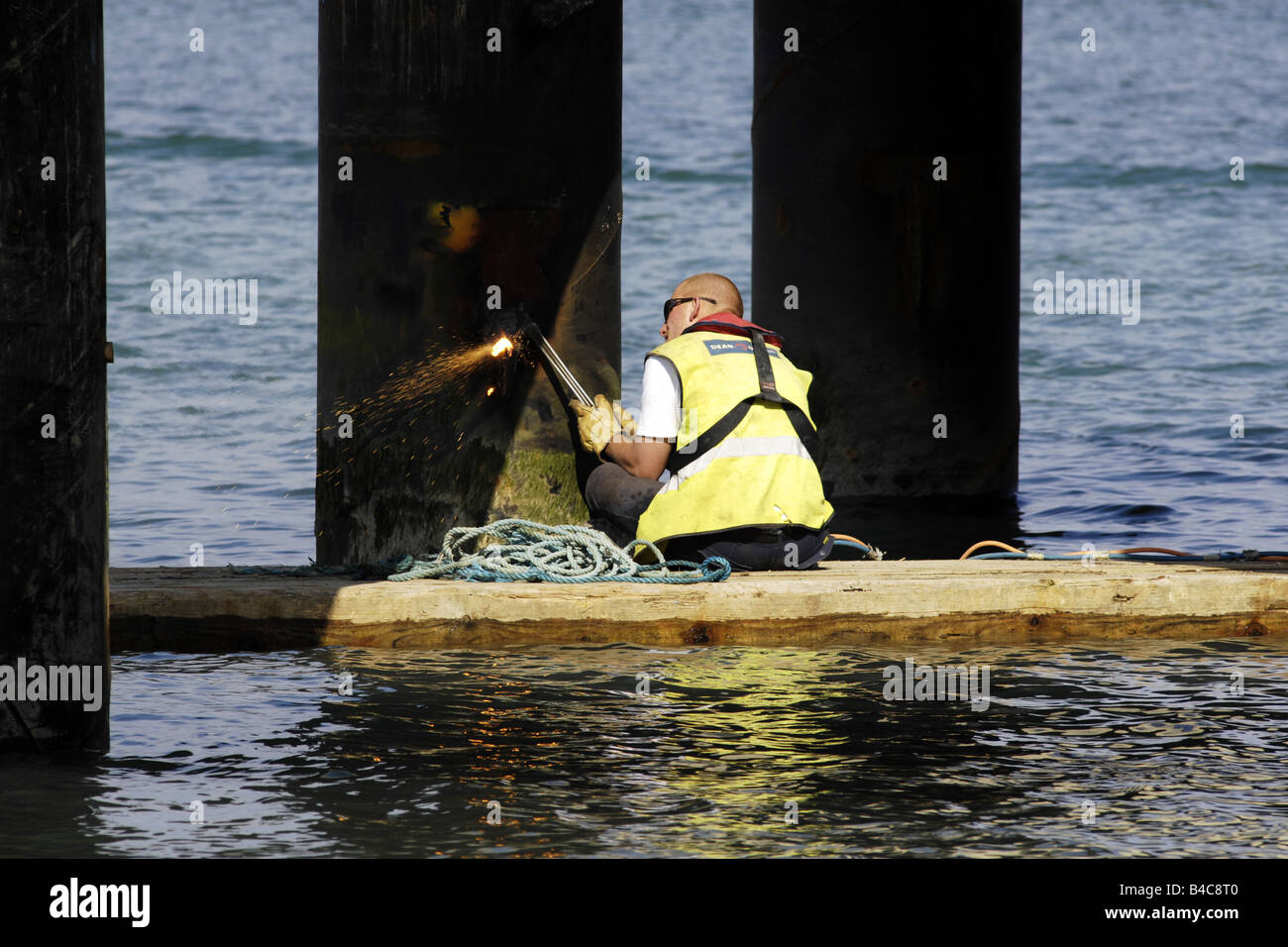 Workman sitting on a small raft using an gas torch to cut and weld a ...