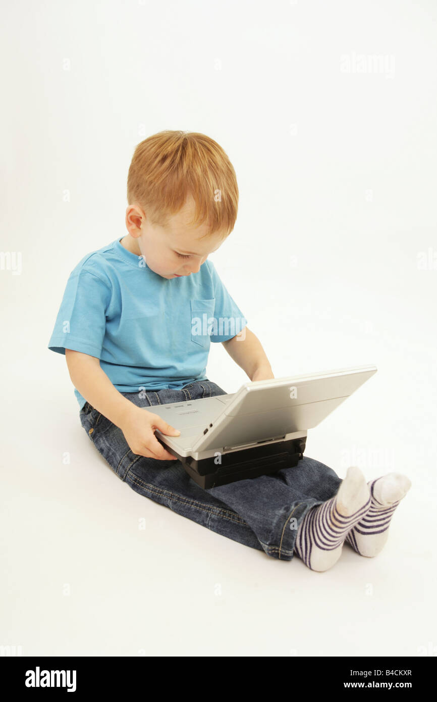 Two year old boy sitting down watching a DVD on his portable DVD player ...