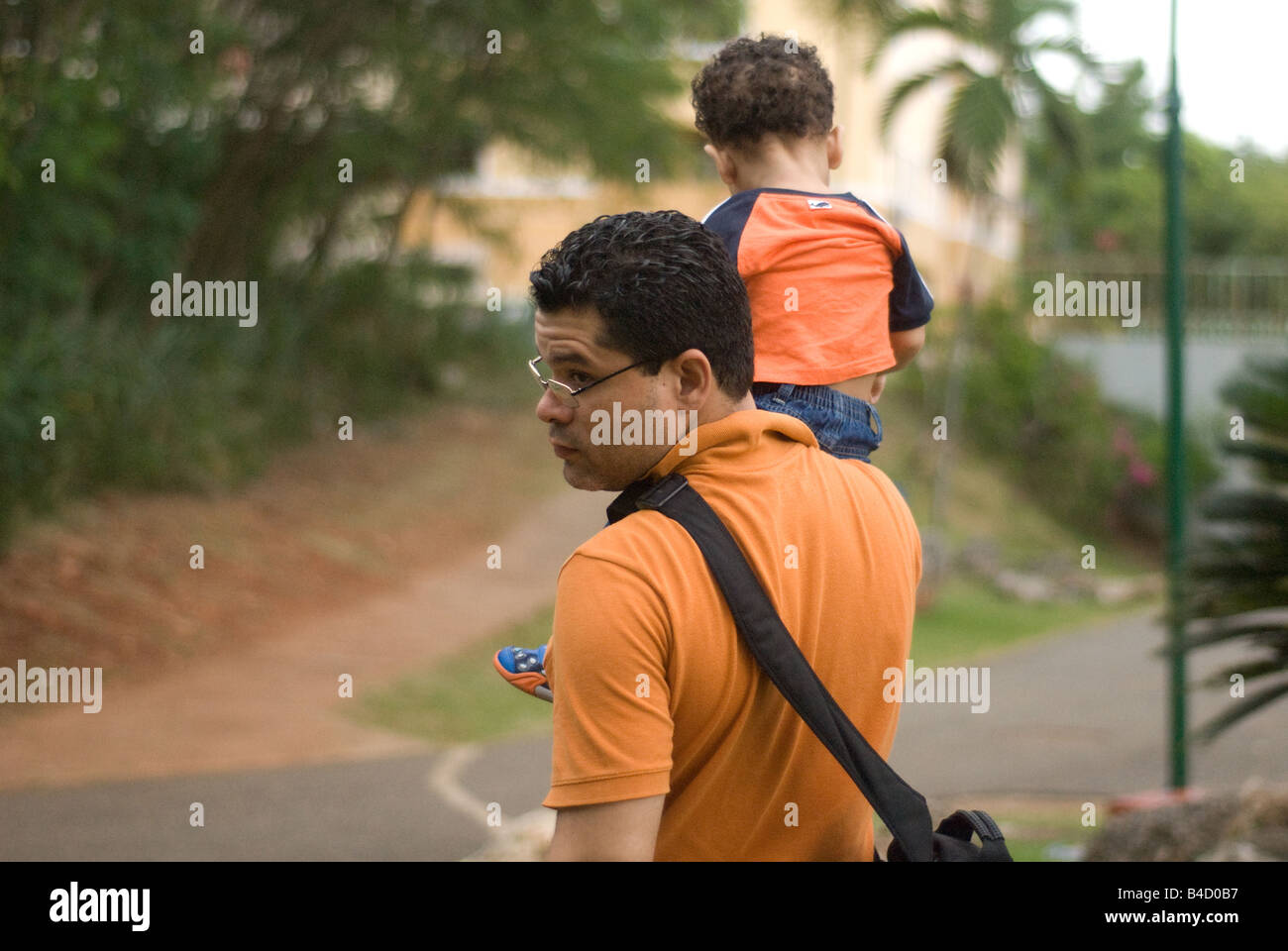 A Latin father walks with his toddler having him over his shoulder, and ...