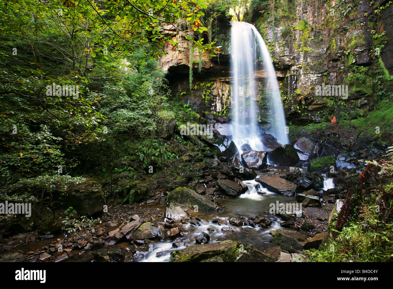 Single waterfall flows falls onto over river bed rocks surrounded by ...