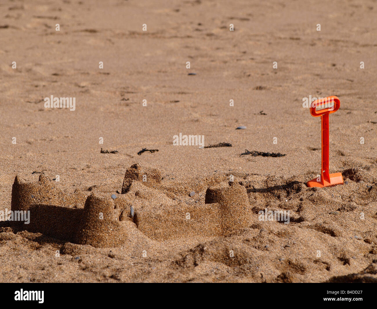 Orange child's plastic spade dug into the sand beside a small sand ...