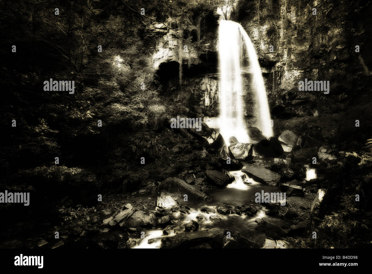 Single waterfall flows falls onto over river bed rocks surrounded by ...