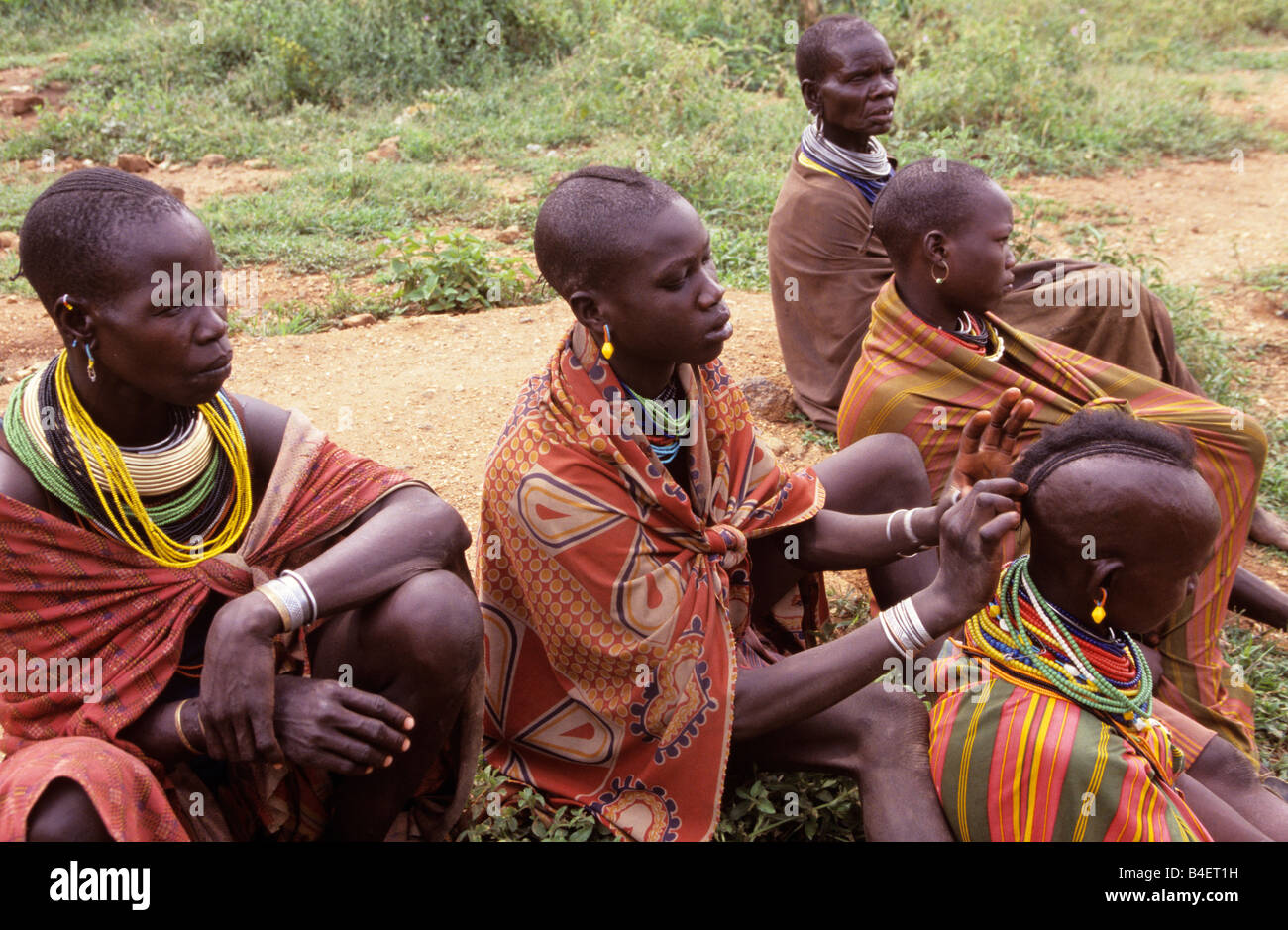 Ethnic Karamojong tribeswomen wearing traditional costume braiding each ...