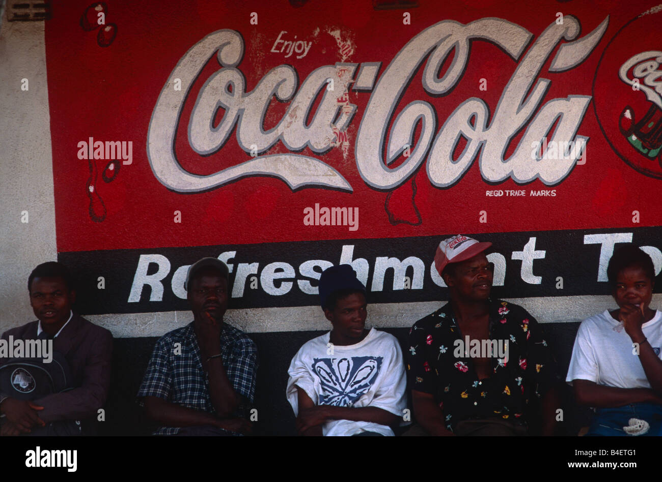 People sitting beneath an advertising sign in Uganda Stock Photo - Alamy