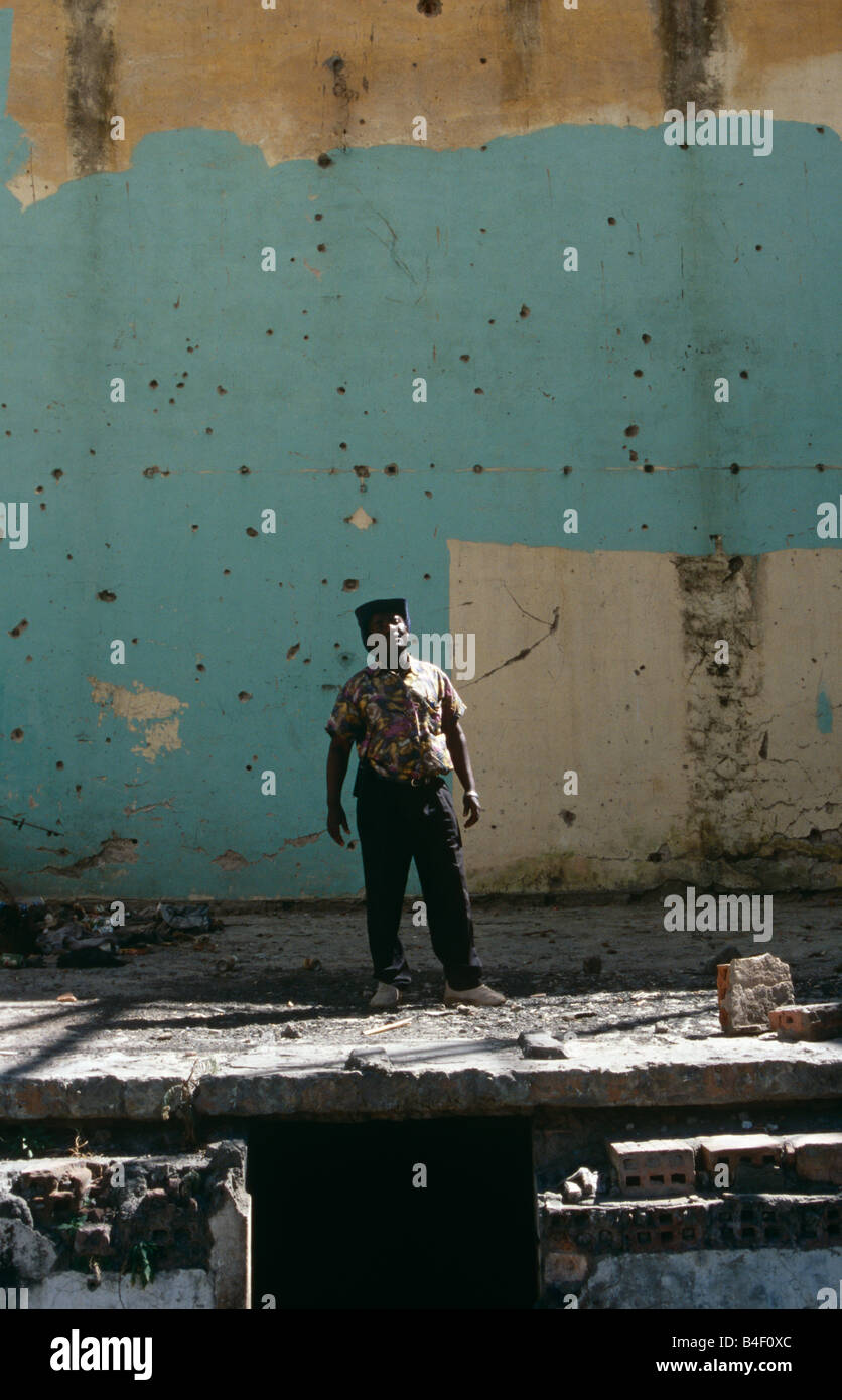 A man standing in front of a bullet-riddled wall in war-ravaged Angola ...