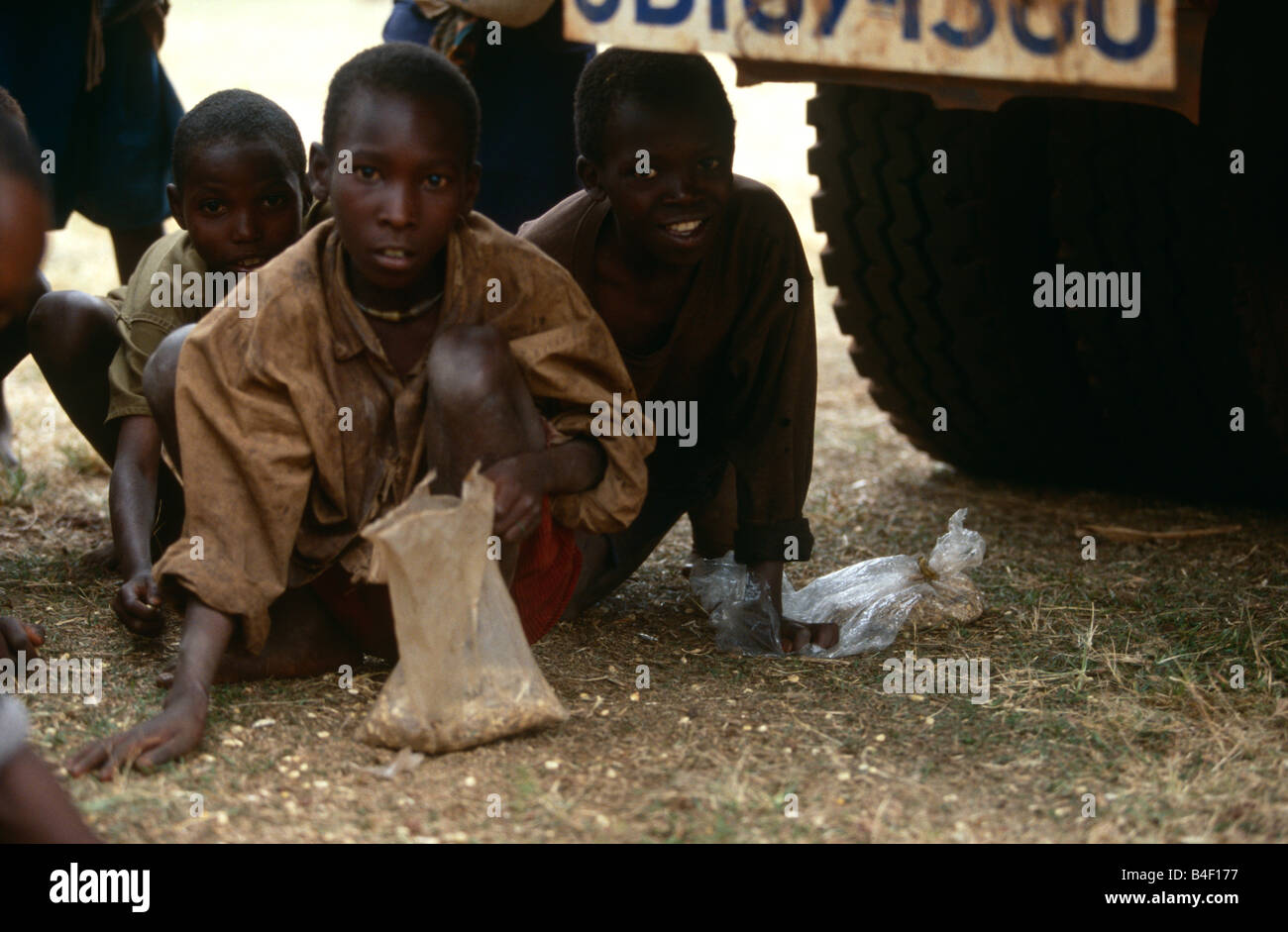 Boys picking up food from ground beside vehicle, Burundi Stock Photo ...