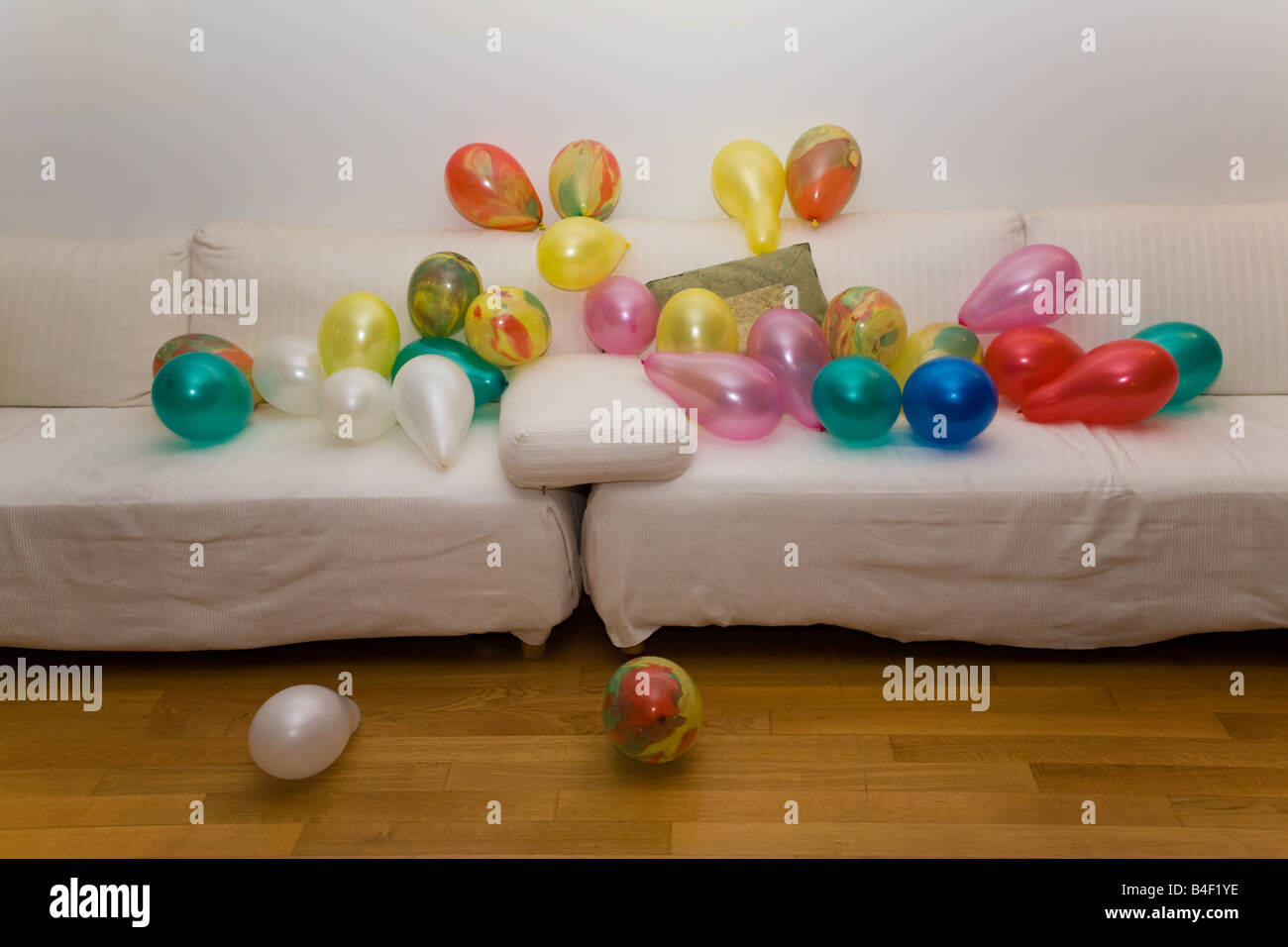 A colorful bunch of party balloons scattered on a white sofa and a ...