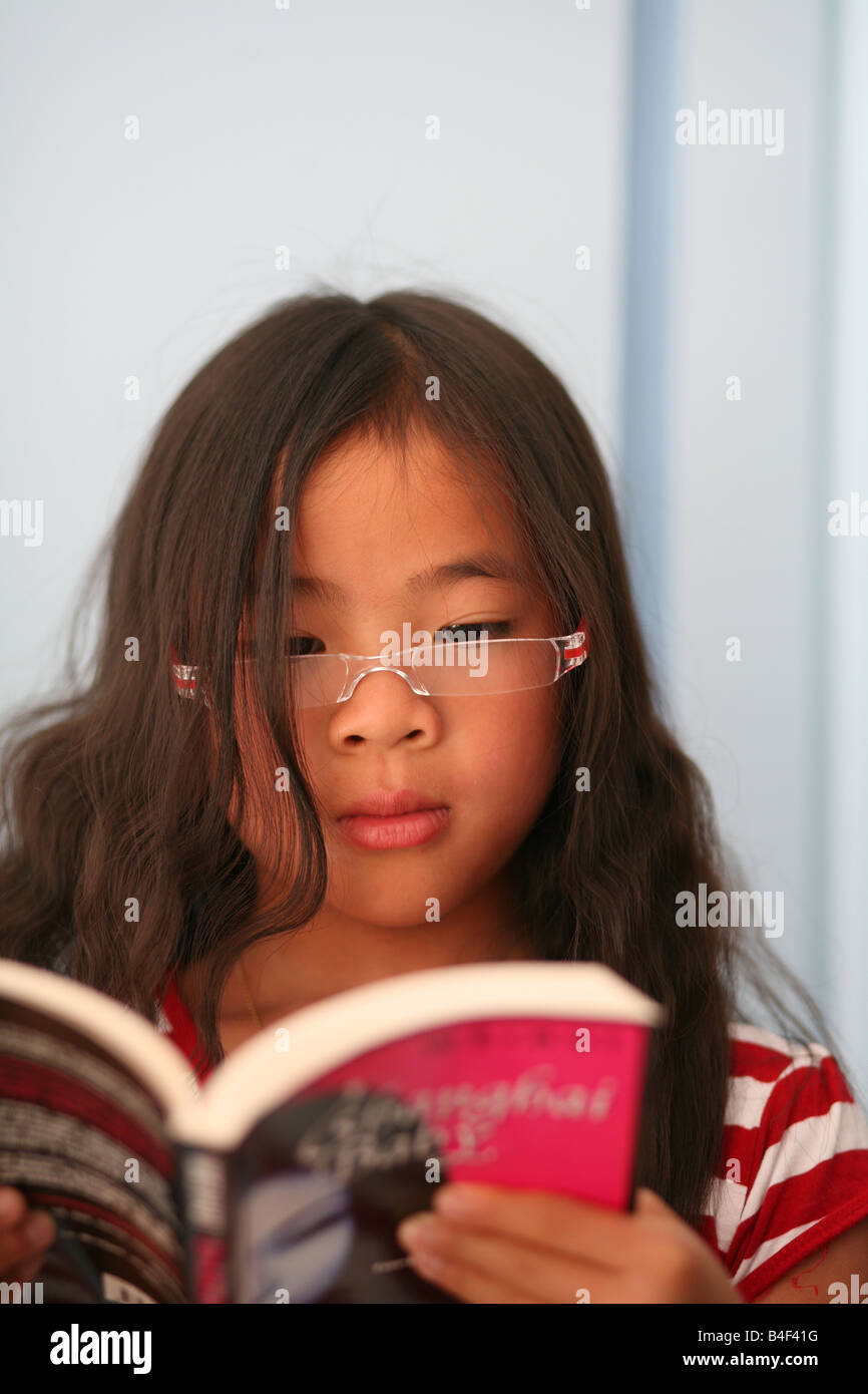 chinese child (girl aged of 8 ) with glasses reading a book and ...