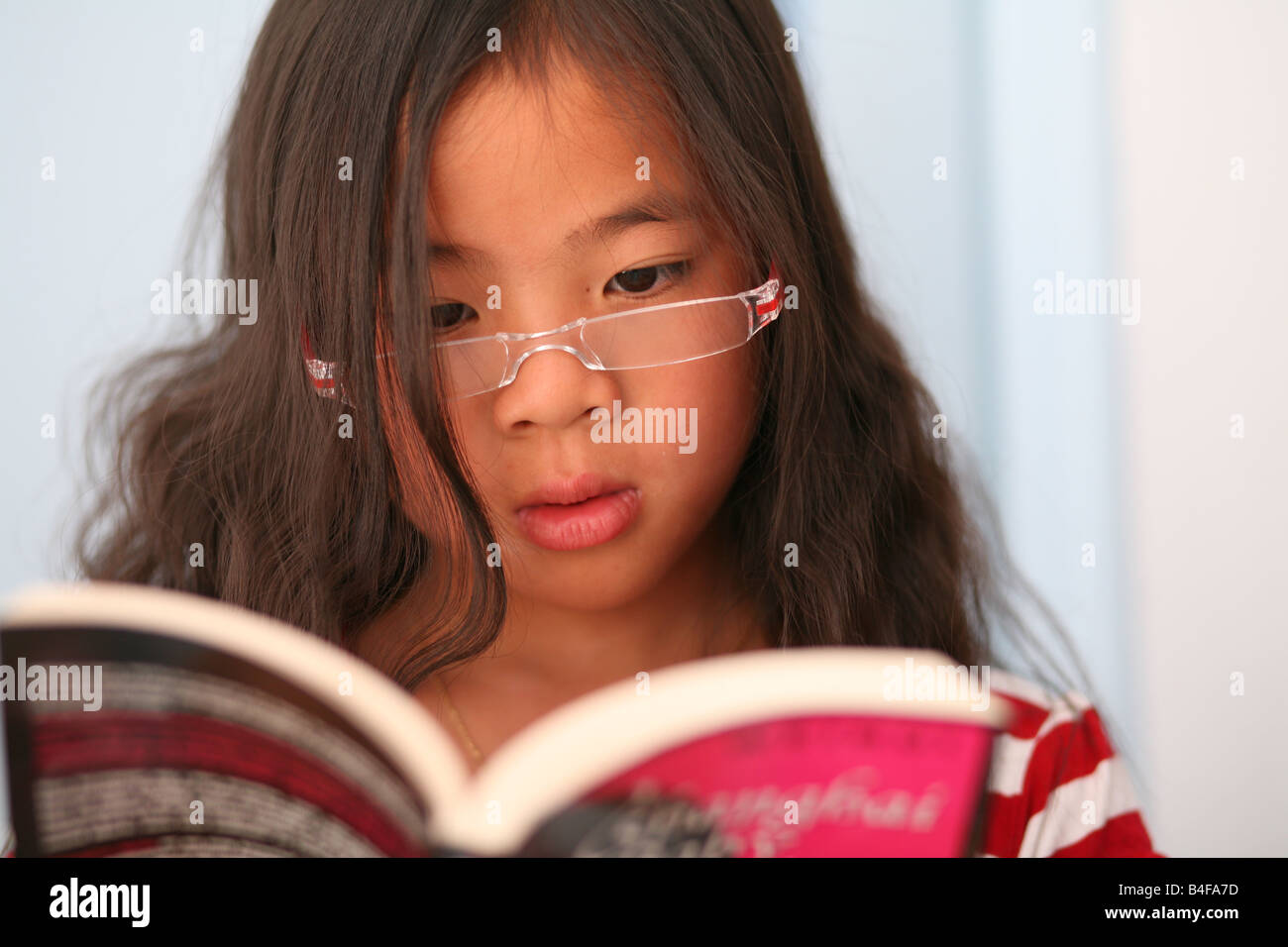 chinese child (girl aged of 8 ) with glasses reading a book and ...