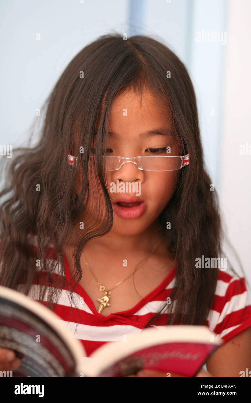 chinese child (girl aged of 8 ) with glasses reading a book and ...
