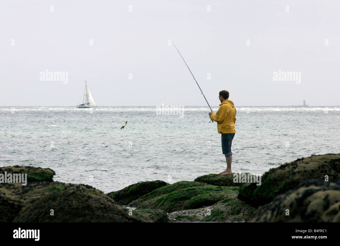 a fisherman stands on rocks catching fish from the ocean Stock Photo ...