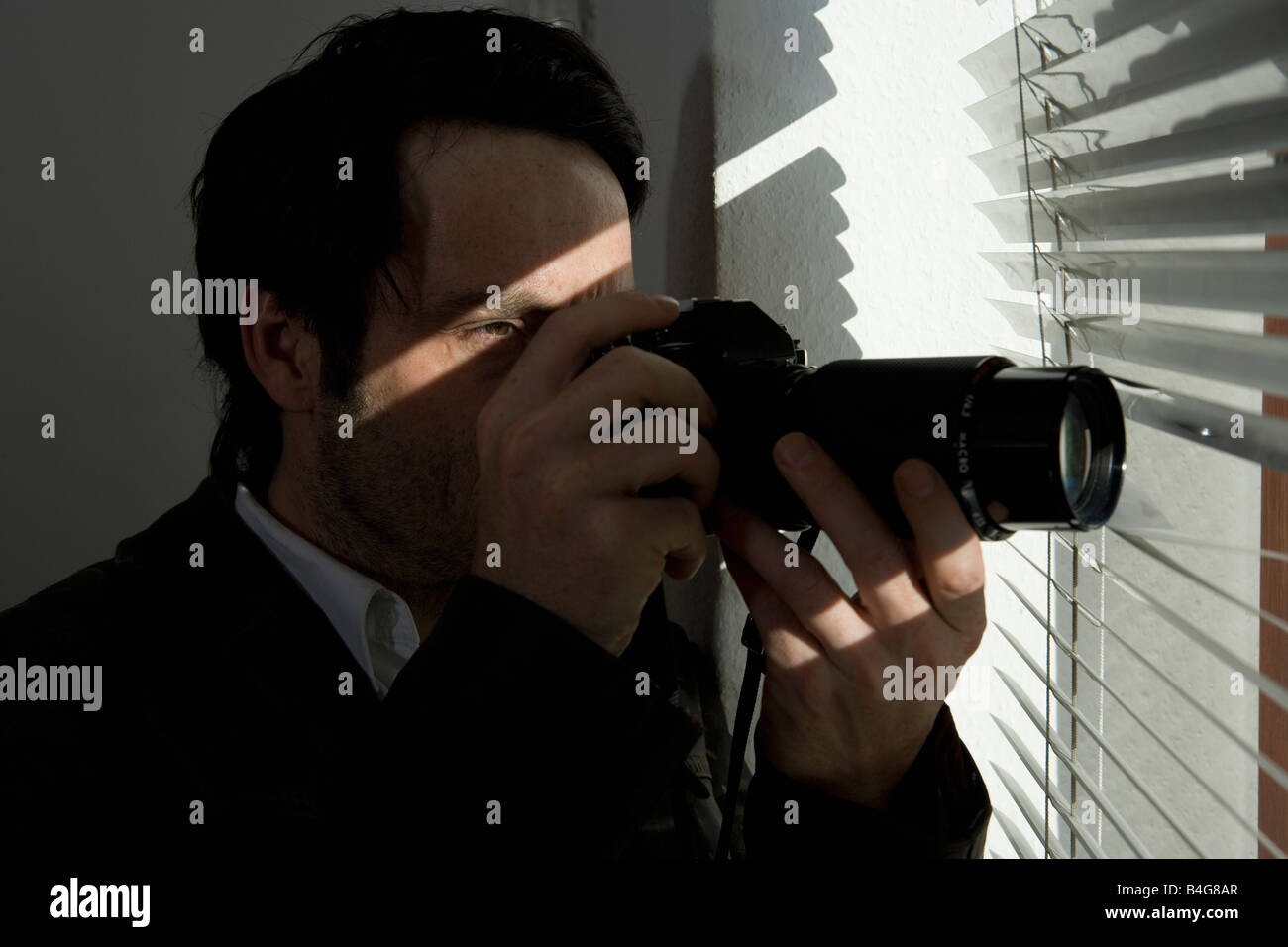 A man looking through blinds with a camera Stock Photo - Alamy