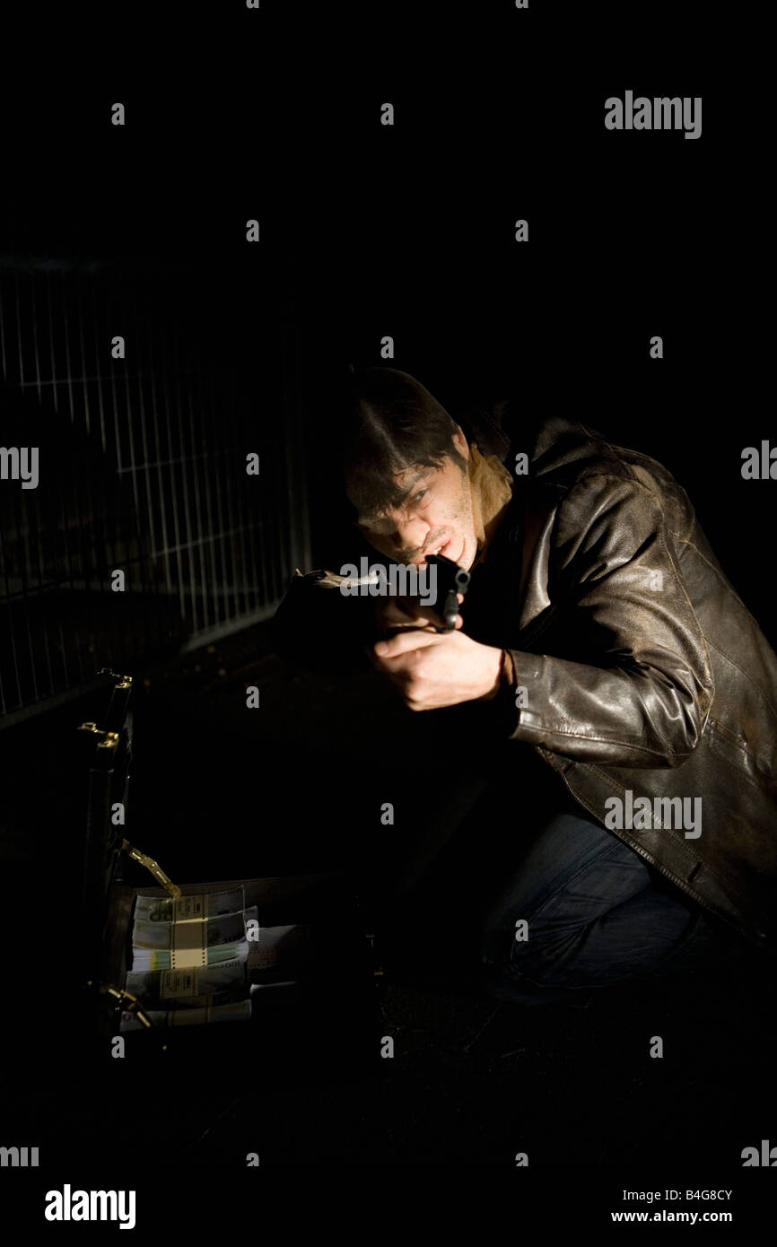 A man with a nylon over his face aiming a gun with a briefcase full of ...