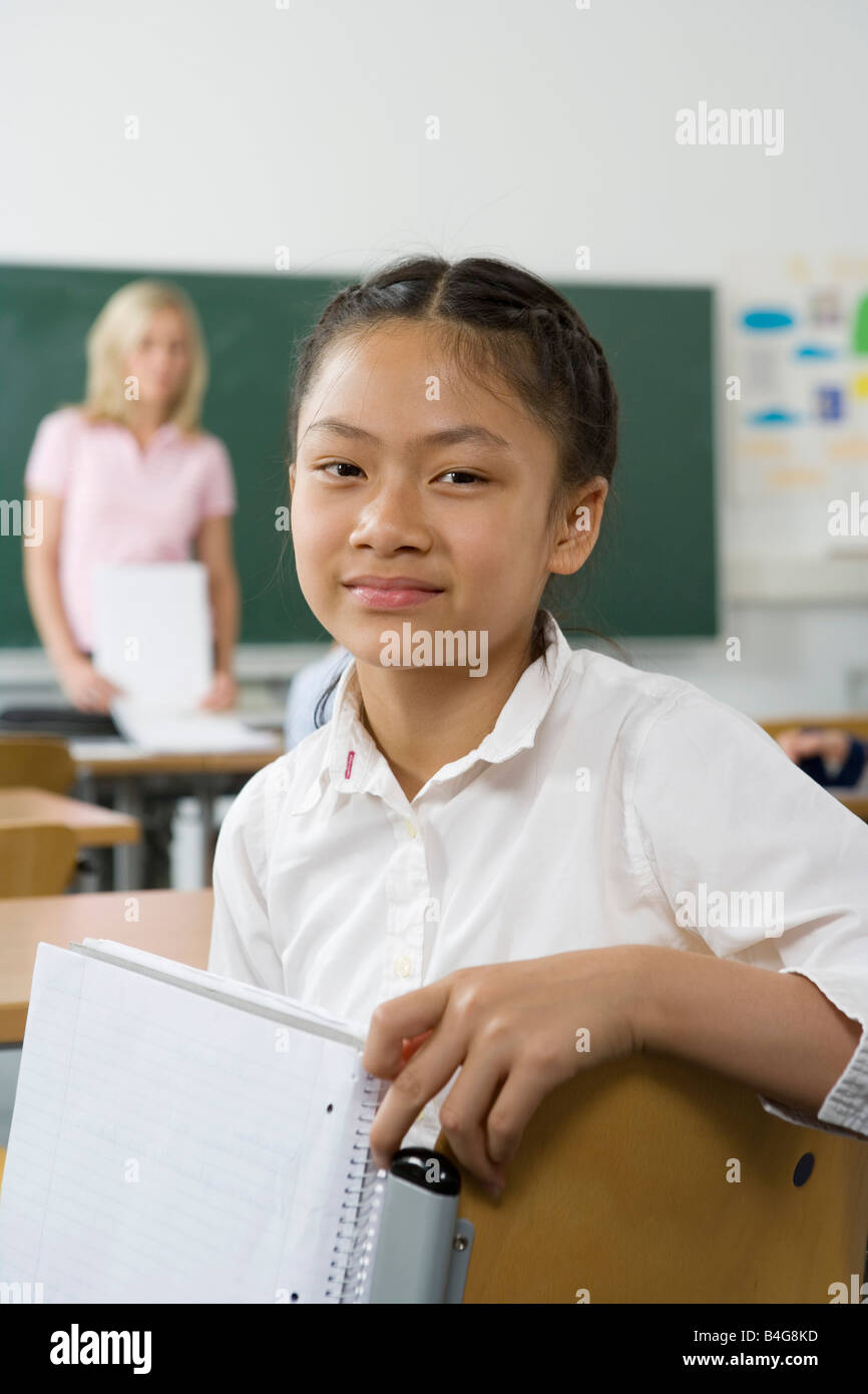 A pre-adolescent girl sitting in the back of a classroom, looking at ...