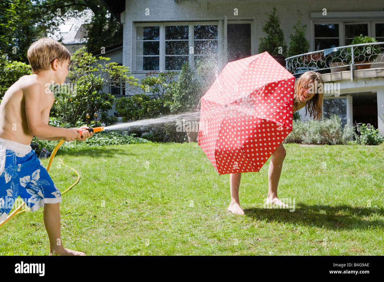 A young boy spraying at his sister with a garden hose Stock Photo - Alamy