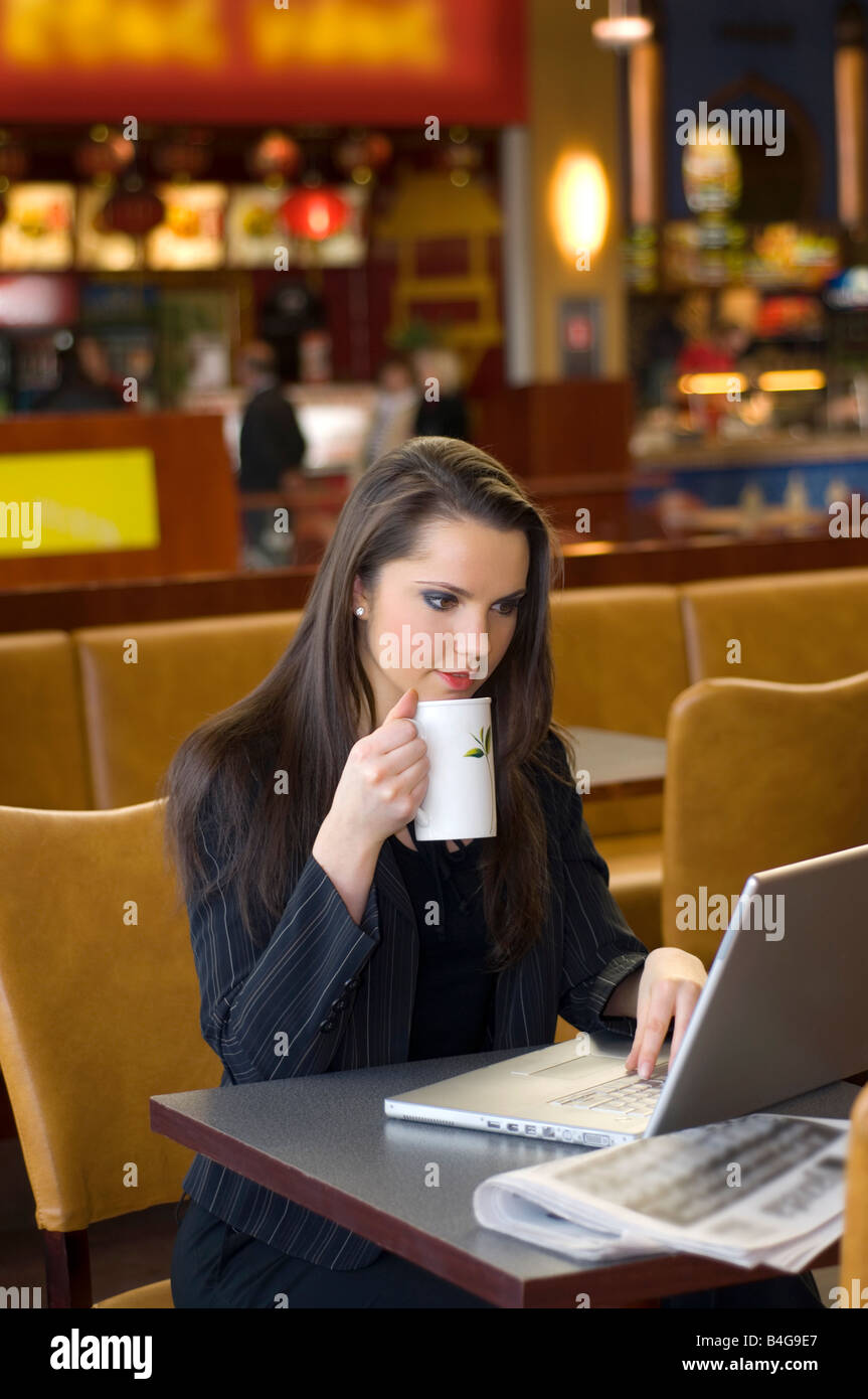 young woman sitting in a cafe drinking a cup of tea working on laptop ...