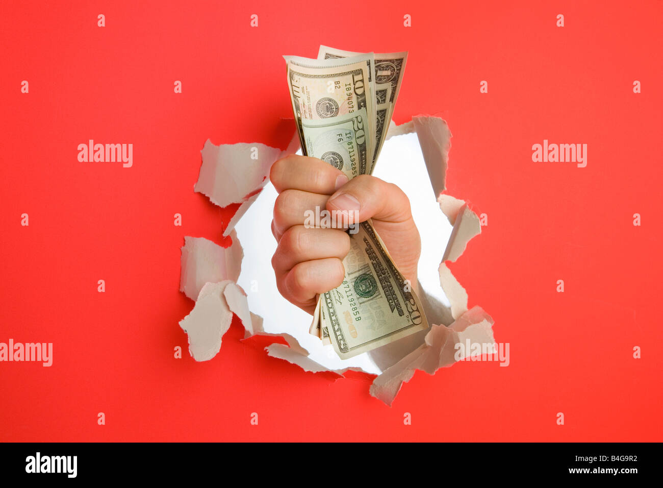 A fist breaking through a wall holding dollar bills Stock Photo - Alamy