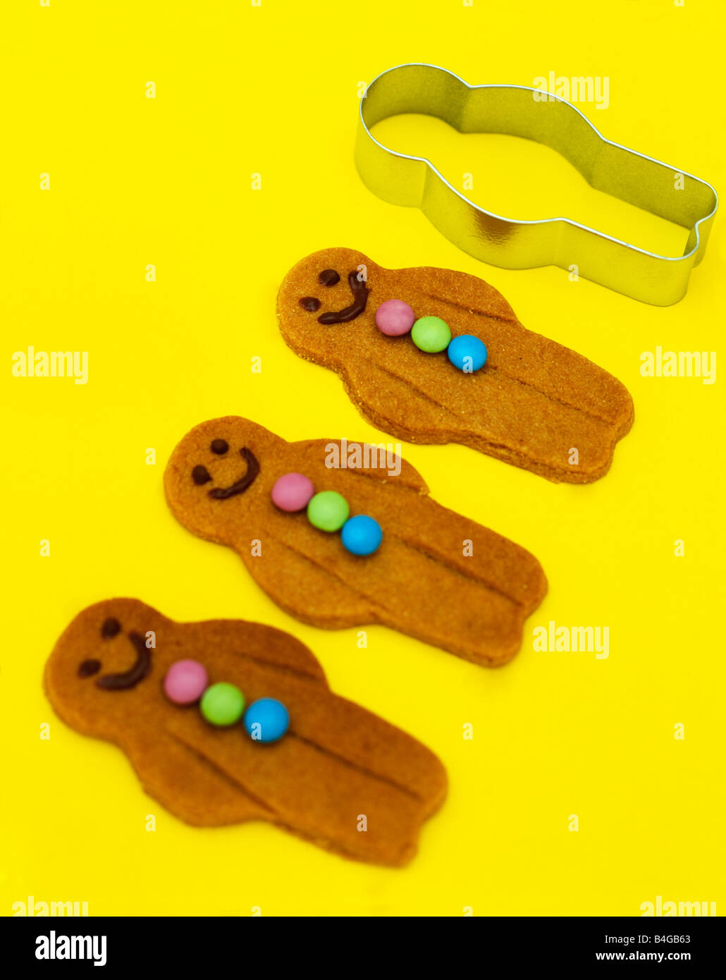 a row of 3 smiling gingerbread men and a mould on a bright yellow ...