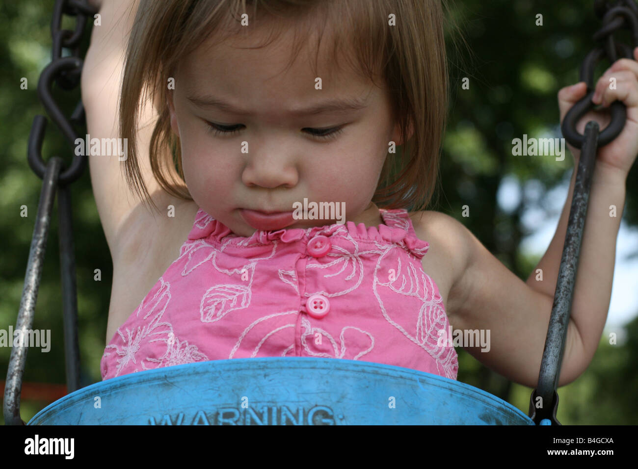 A 21-month-old toddler girl looks down while sitting in a bucket swing ...