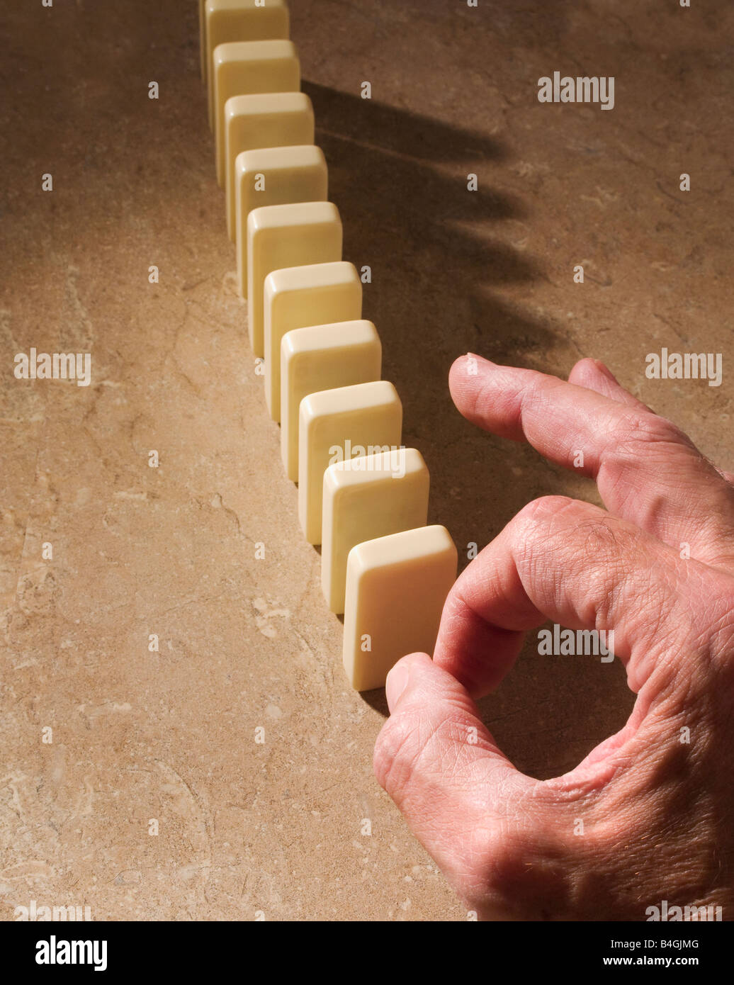close up of hand poised to knock over dominoes Stock Photo - Alamy
