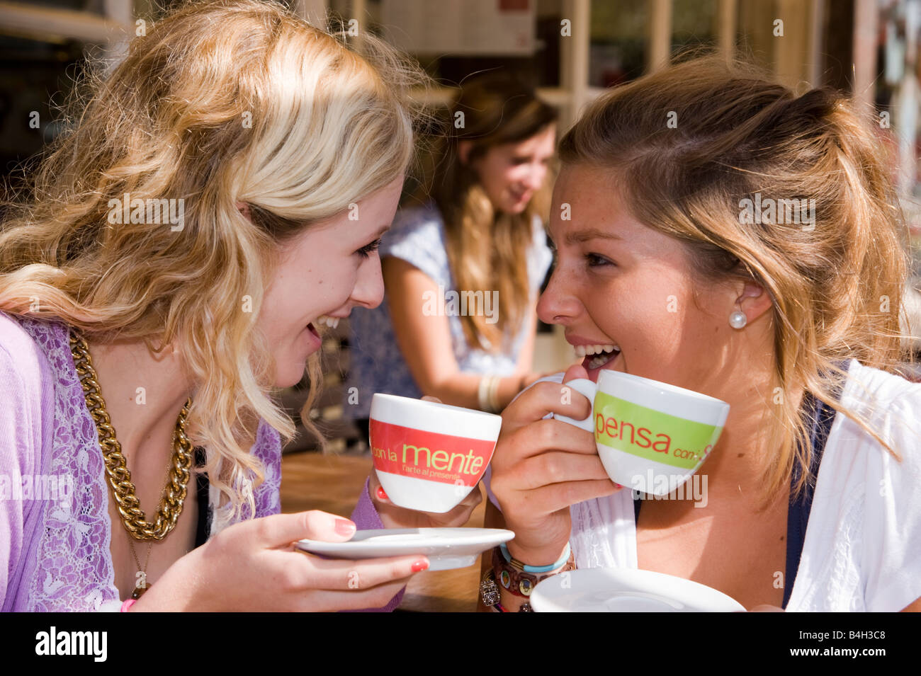 2 teenage girls laughing and chatting over a coffee at an outdoor cafe ...
