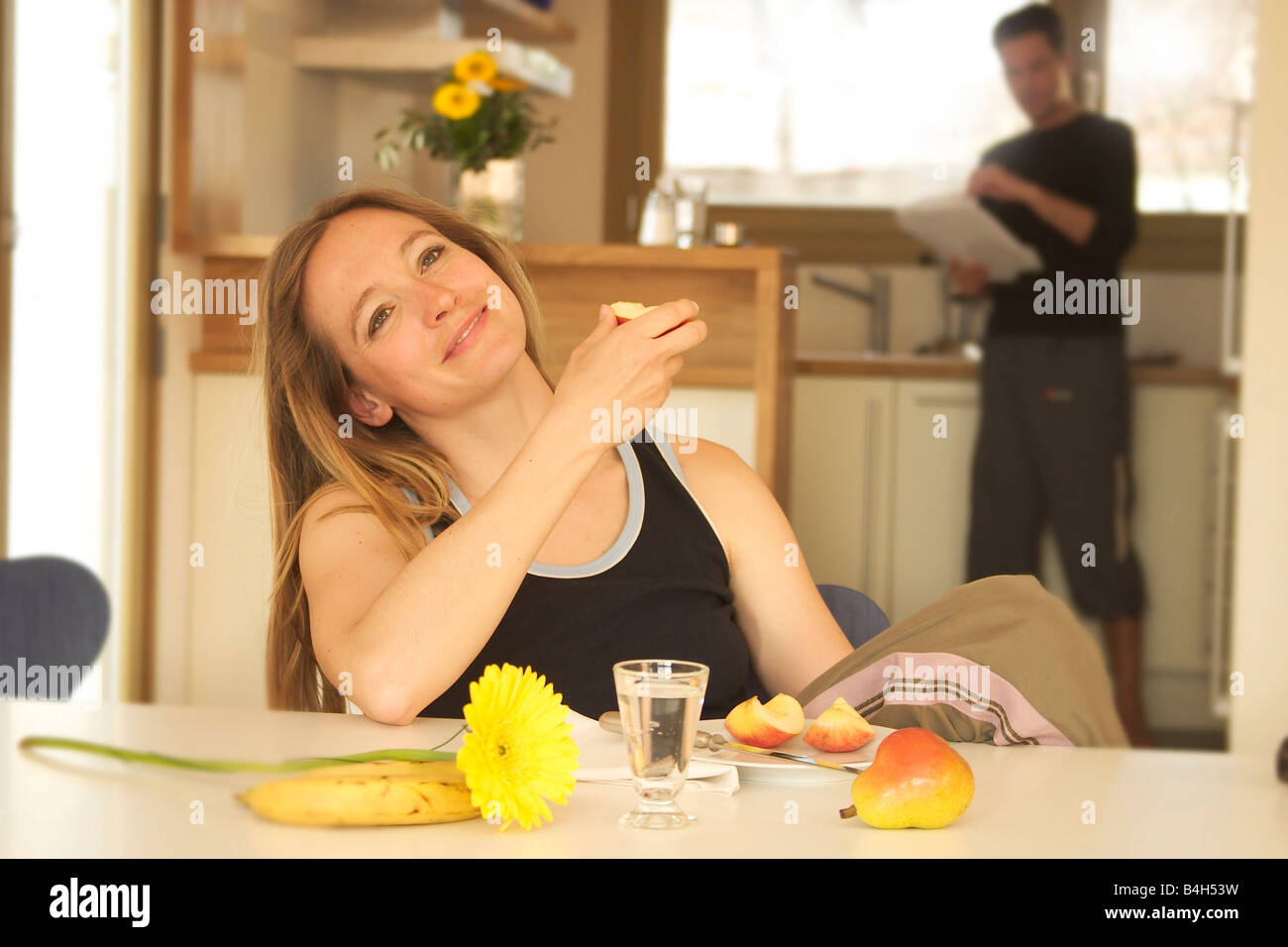 Close-up of young woman eating apple at table with her husband standing ...