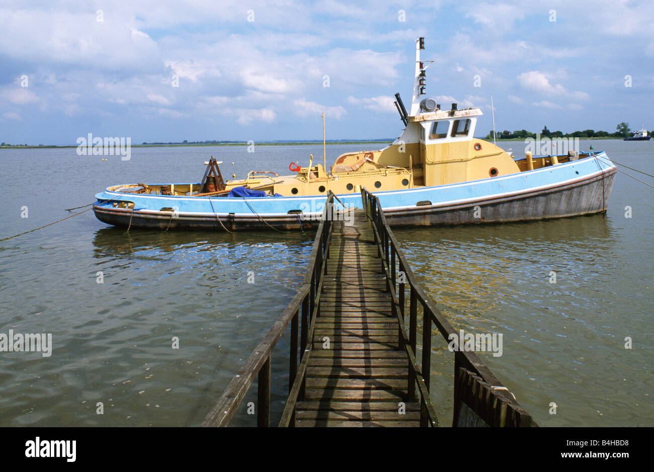 Wooden footbridge to yellow and blue tugboat on the water at Heybridge ...