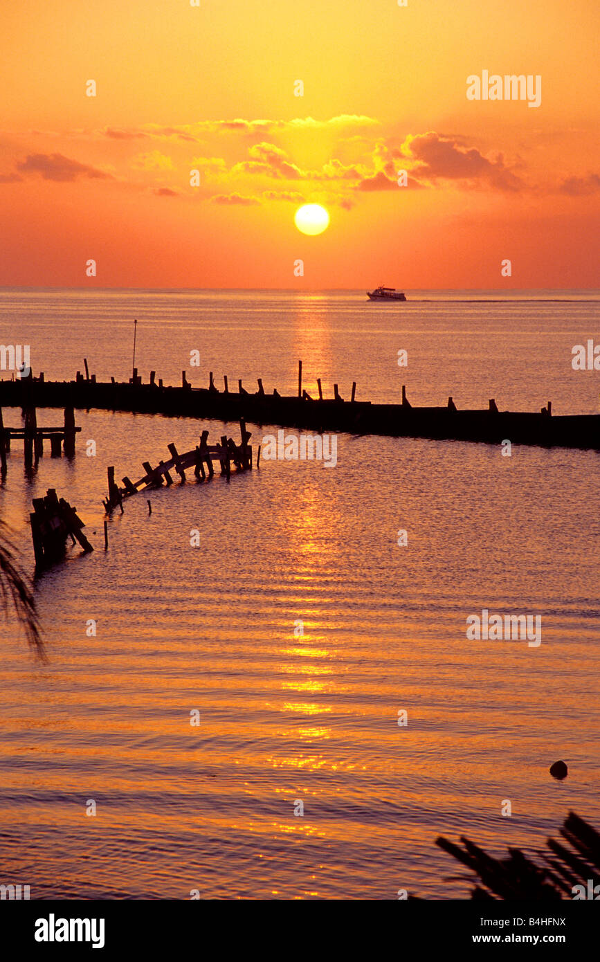 Tropical island sun rises over a pier as a ferry boat crosses the ...
