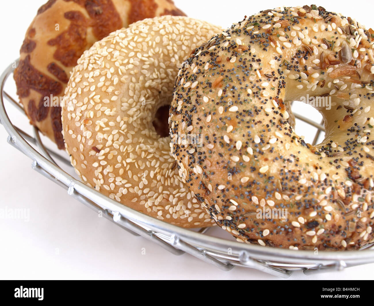 Fresh baked bagels in a wire basket isolated against a white background ...