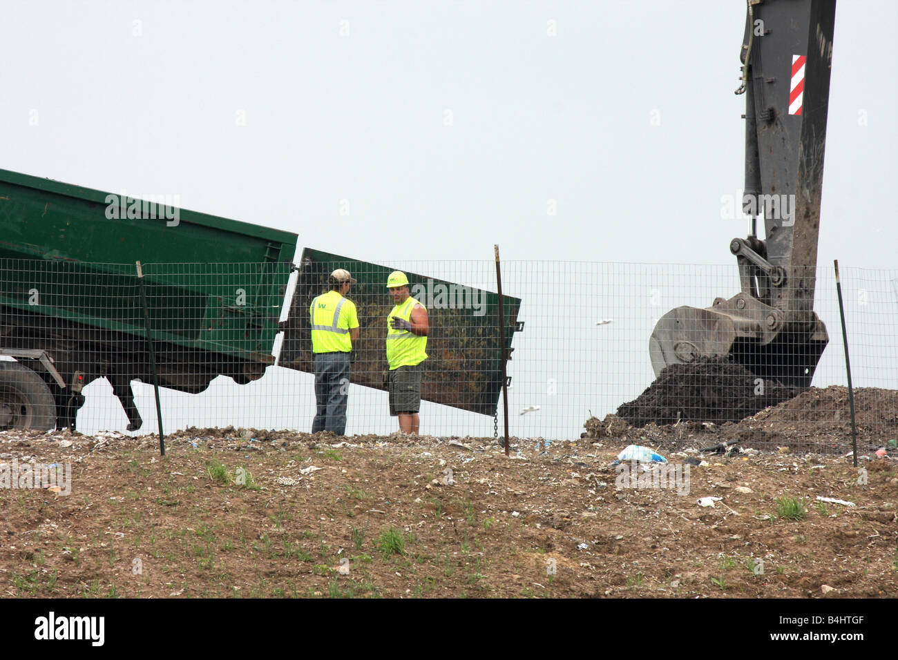 Waste Management Landfill workers with a backhoe placing dirt on trash ...