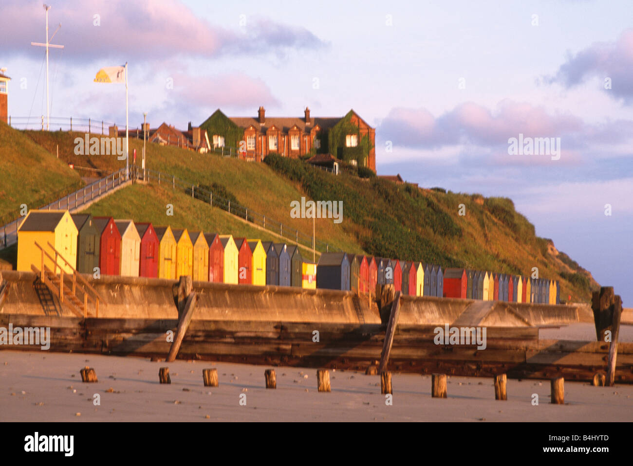 Wooden beach huts below houses on grassy cliff at Mundesley in Norfolk ...
