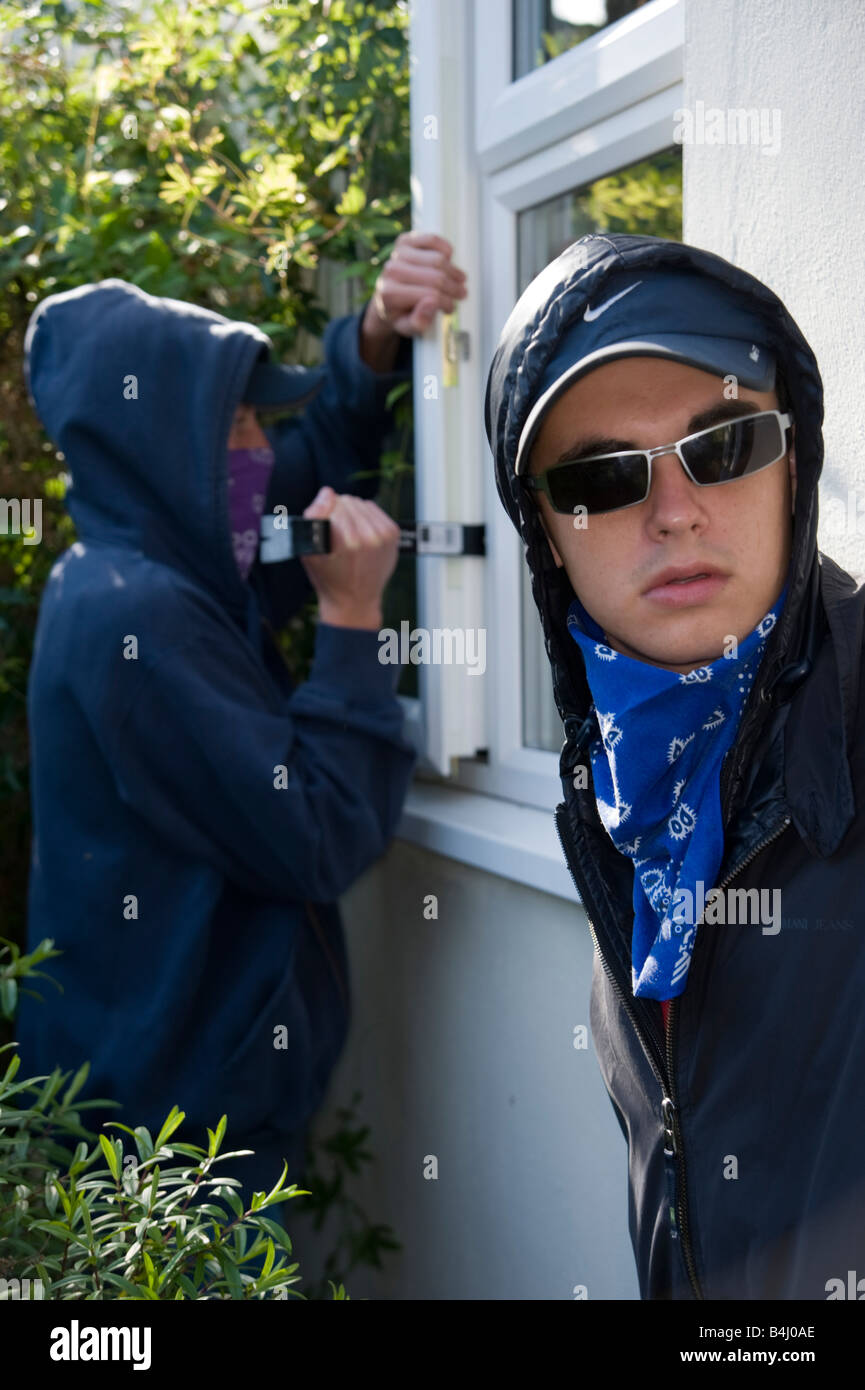 teenage boy winching open a window to break into a house with another ...