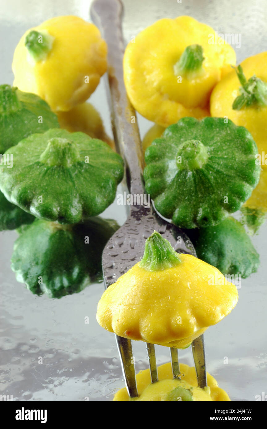 Variety of fresh summer squash pierced with a fork on a reflective ...