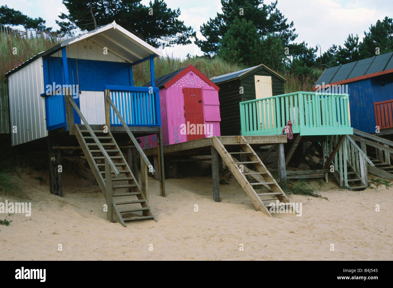 Brightly painted wooden beach huts with wooden ladders on a sandy beach ...