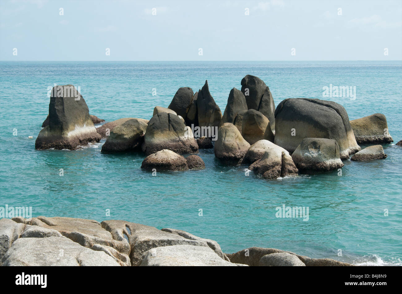 A rock formation poking up through the azure waters off the coast of ...