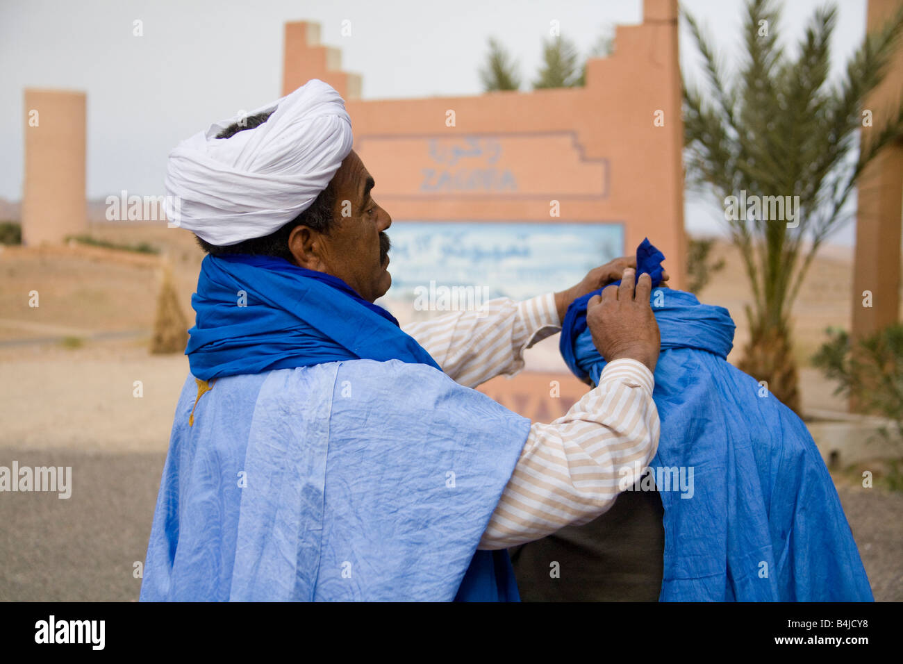Merchant trader putting on head cover turban on tourist head Zagora ...