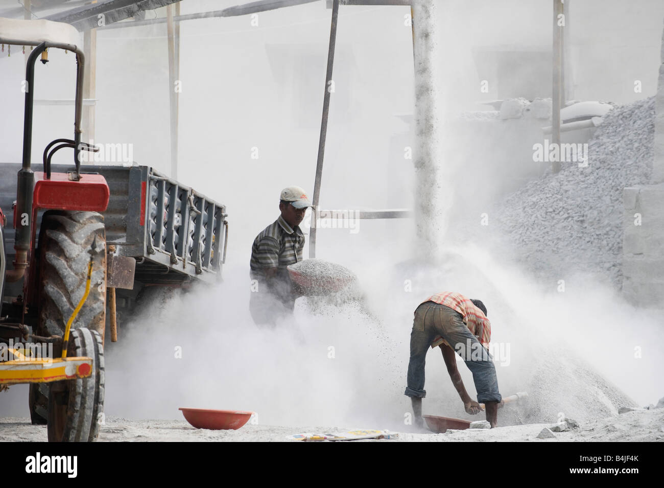 Indian men putting crushed stone into a trailer, surrounded by dust ...